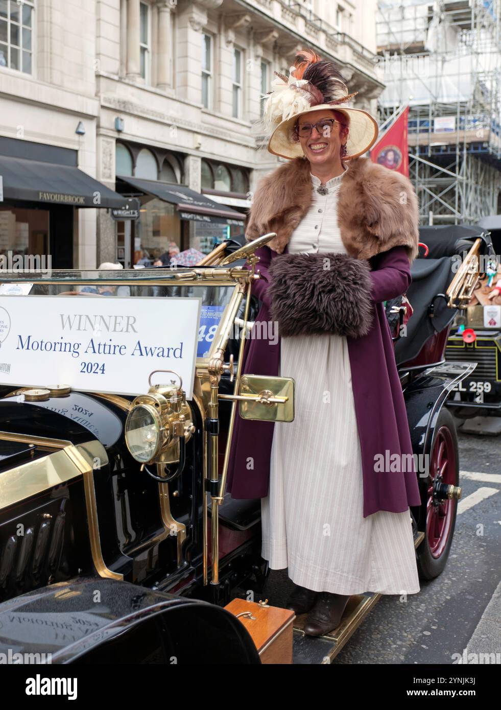 Smiling women in period costume poses by a veteran car after winning ...