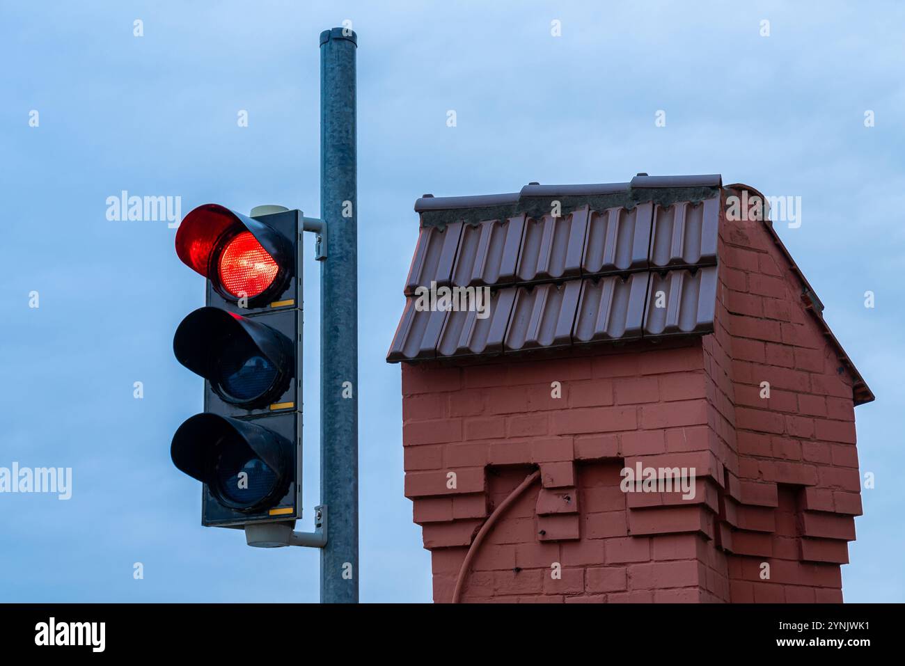 A red traffic light hangs alongside a brown brick structure with a ...