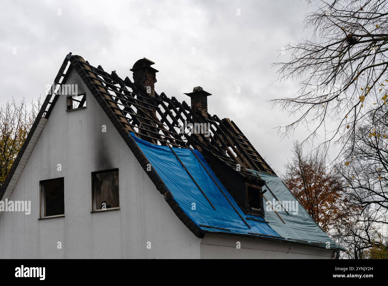 A building shows significant roof damage with a blue tarp covering ...