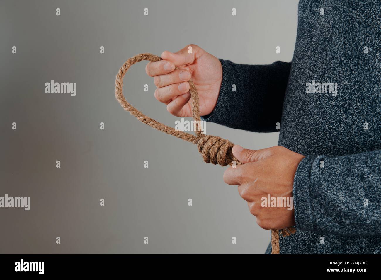a man holds a jute rope with a noose, on a gray background with some ...