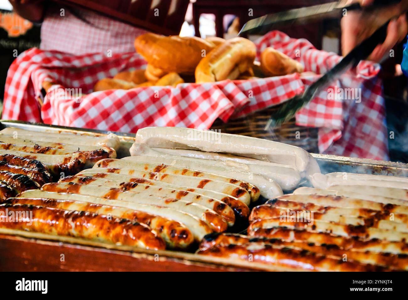 Sausages on the grill, hands of the seller and a pile of buns at ...
