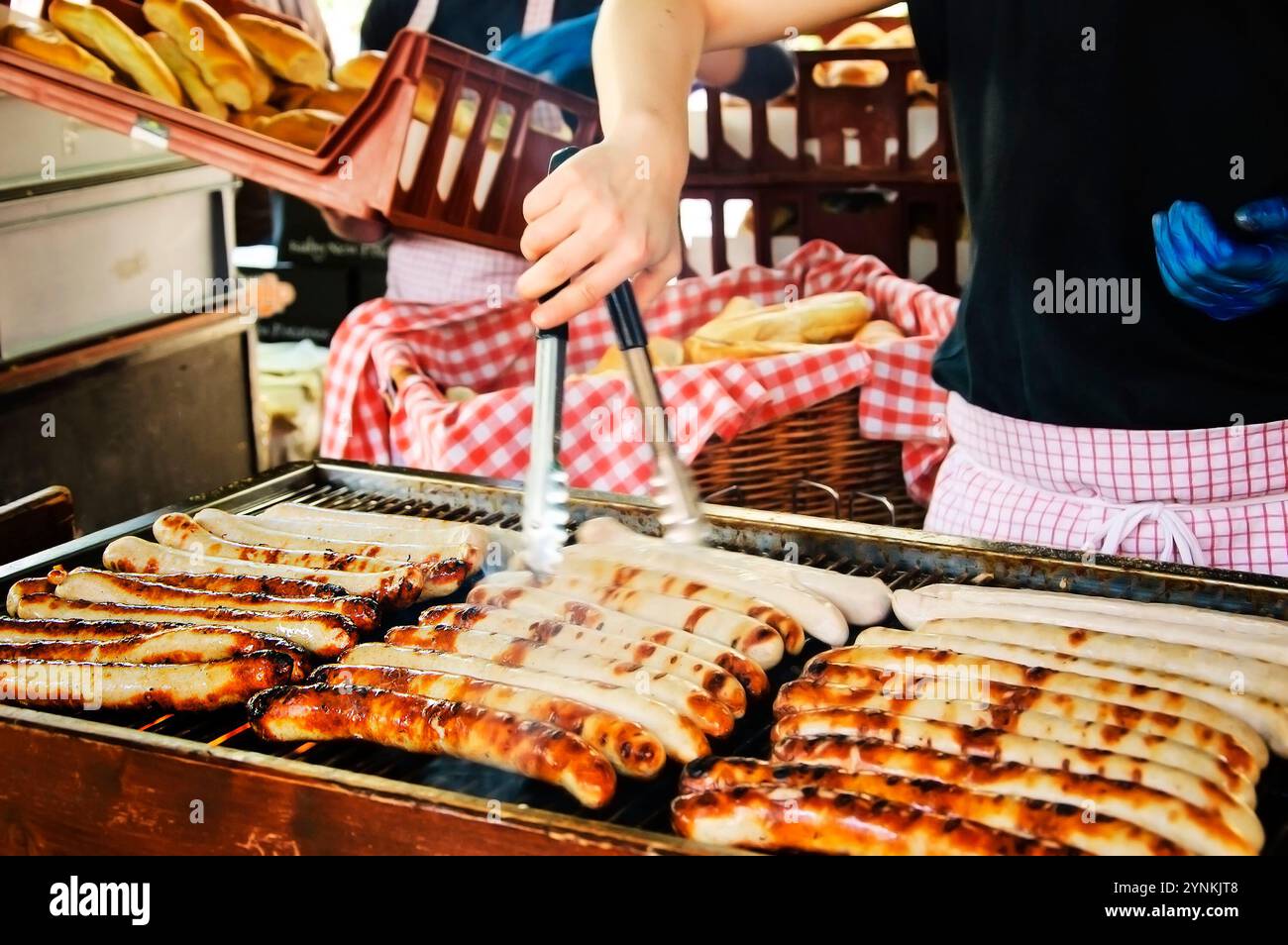 Sausages on the grill, hands of the seller and a pile of buns at ...