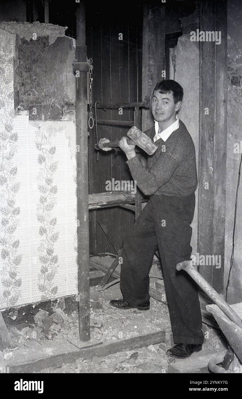 1950s, historical, a man with a sledge hammer knocking down an entrance ...
