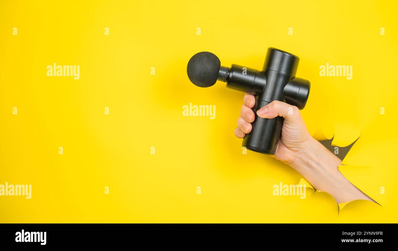 Female hand sticking out with massage gun from yellow paper background ...