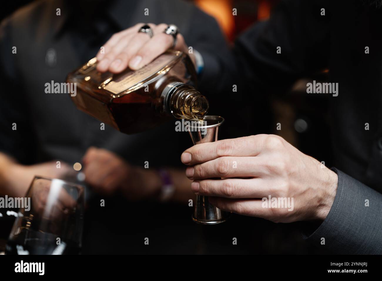 Bartender pouring liquor into a jigger in a lively bar setting at night Stock Photo - Alamy