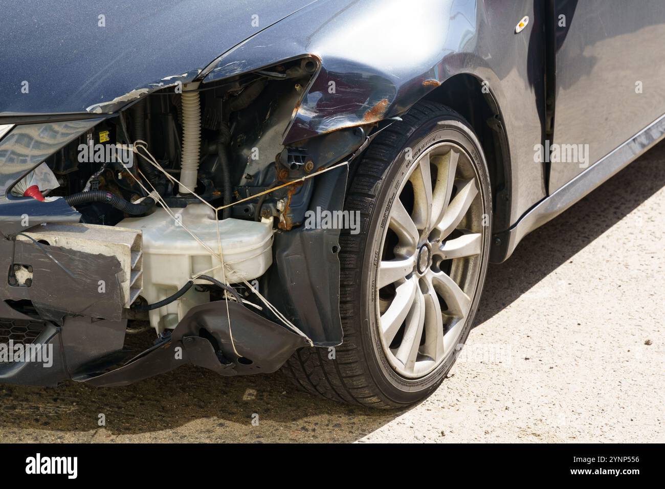A vehicle with a crumpled front bumper and broken parts rests on the ...