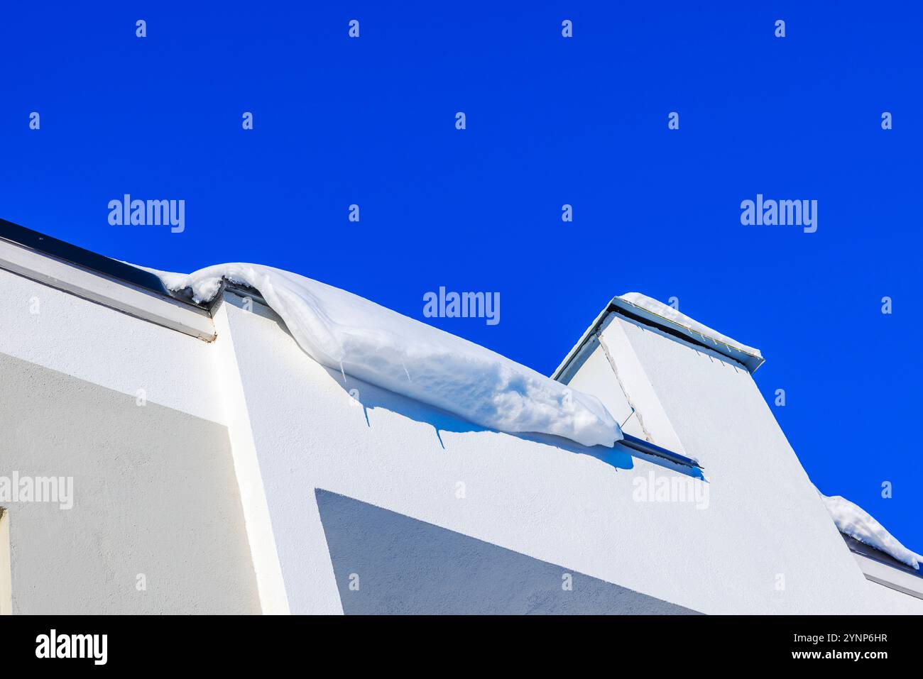 Snow sliding off white building rooftop under vibrant blue winter sky ...