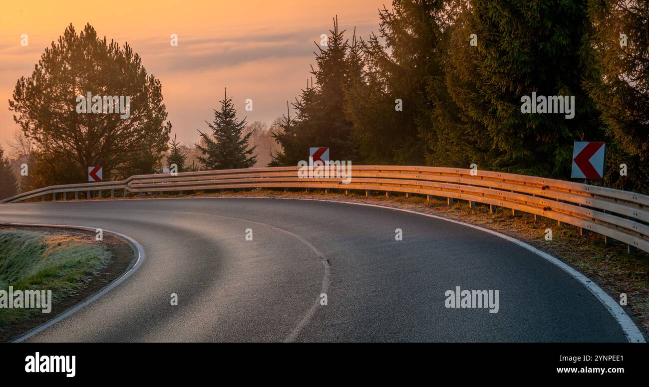 Winding asphalt road with barriers during spectacular sunrise above low ...