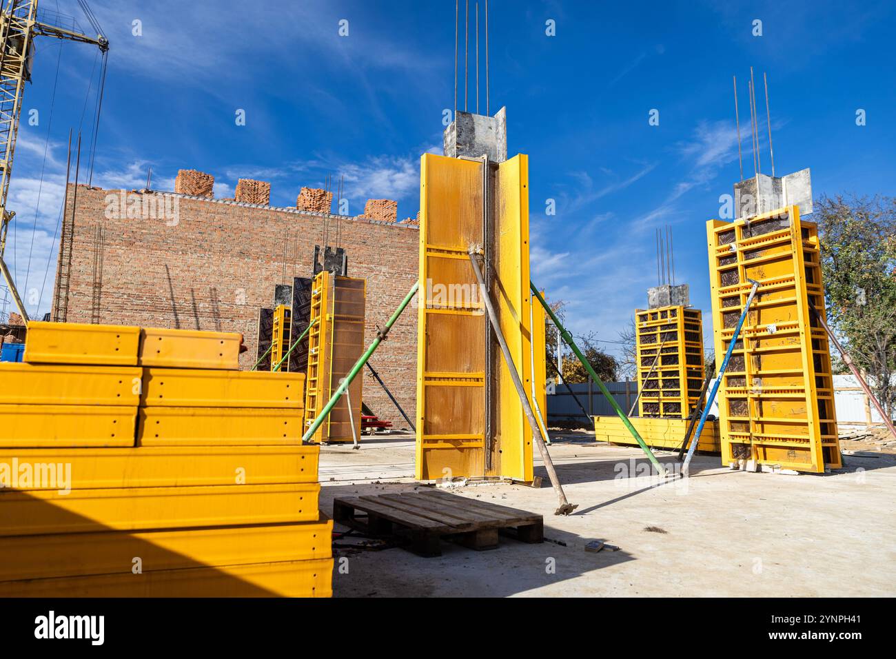 Construction site with yellow formwork, cranes, and materials under a ...