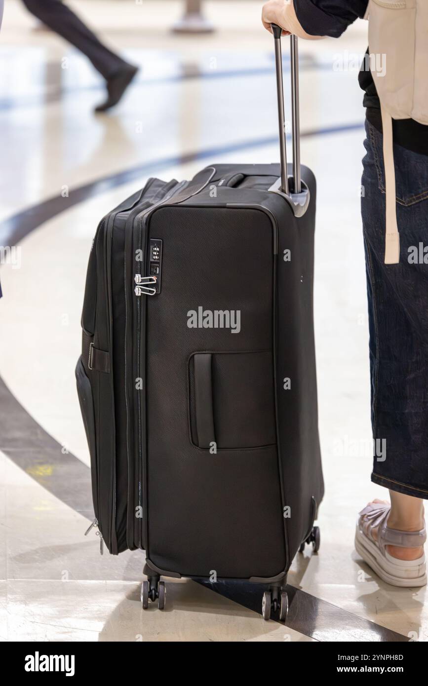 Close-up of a traveler pulling a black rolling suitcase in an airport ...