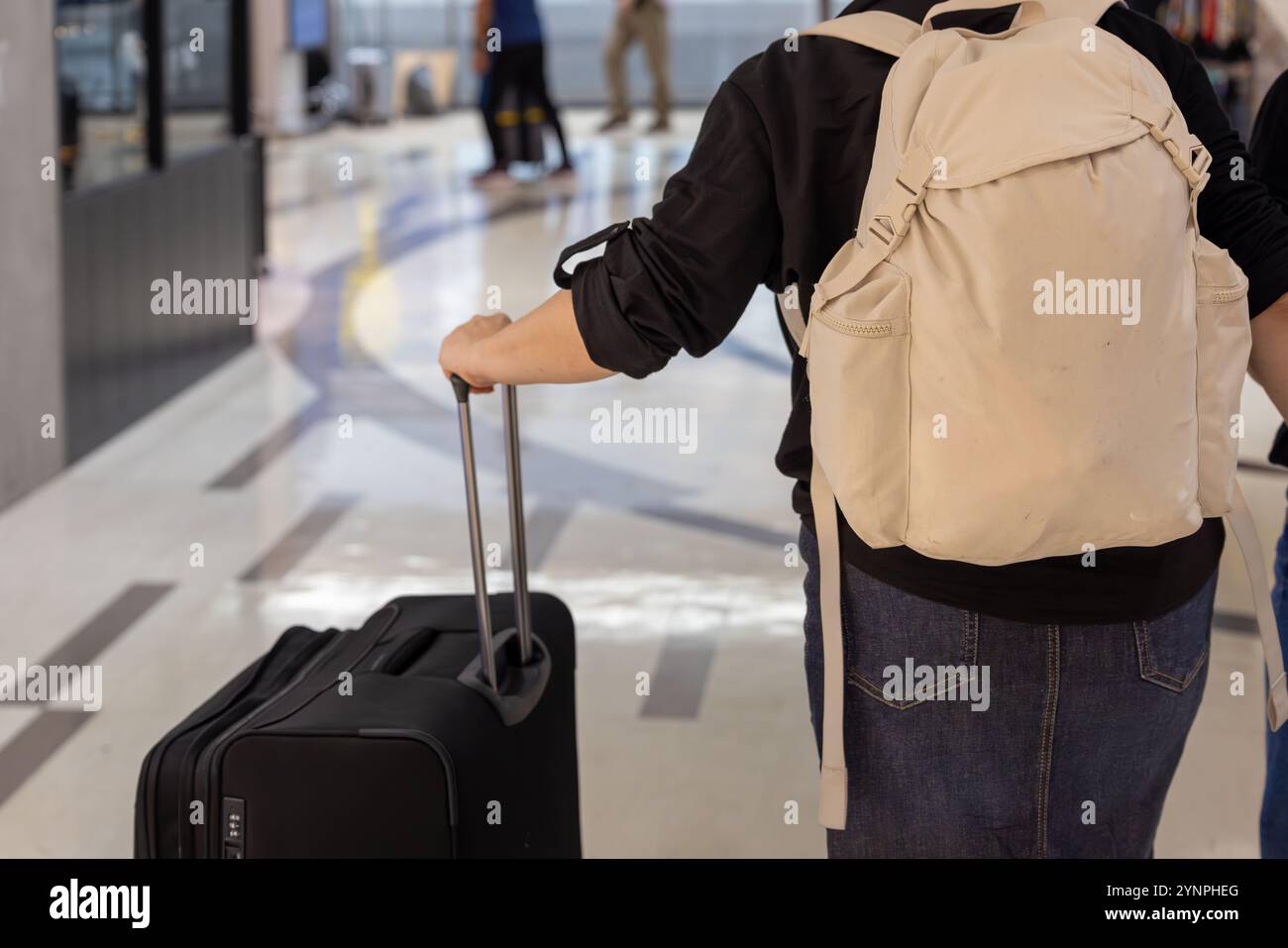 Traveler with a backpack pulling a suitcase in an airport Stock Photo ...