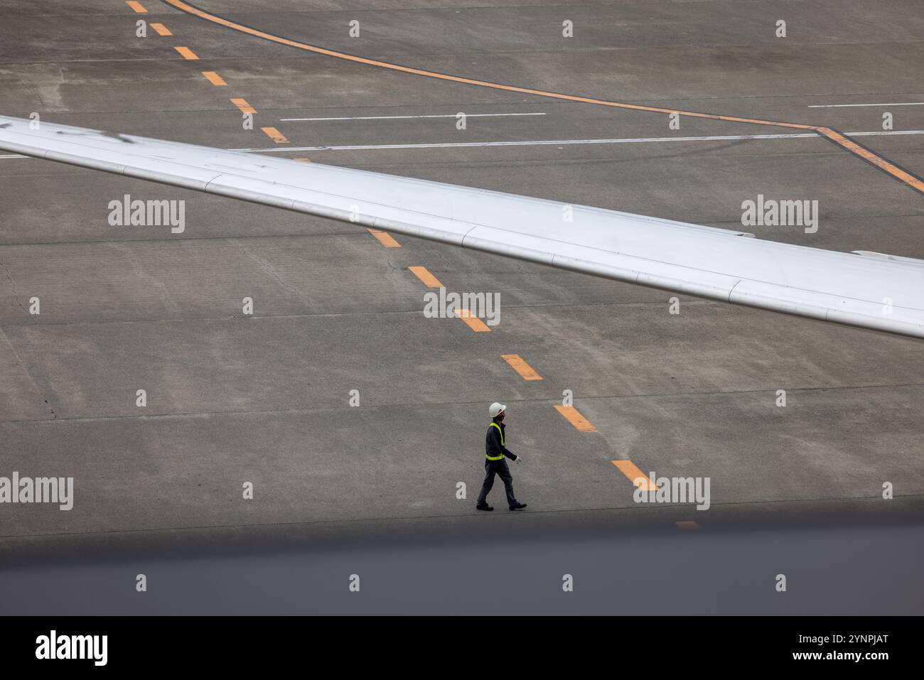 Ground crew member walking beneath an aircraft wing on the tarmac Stock ...