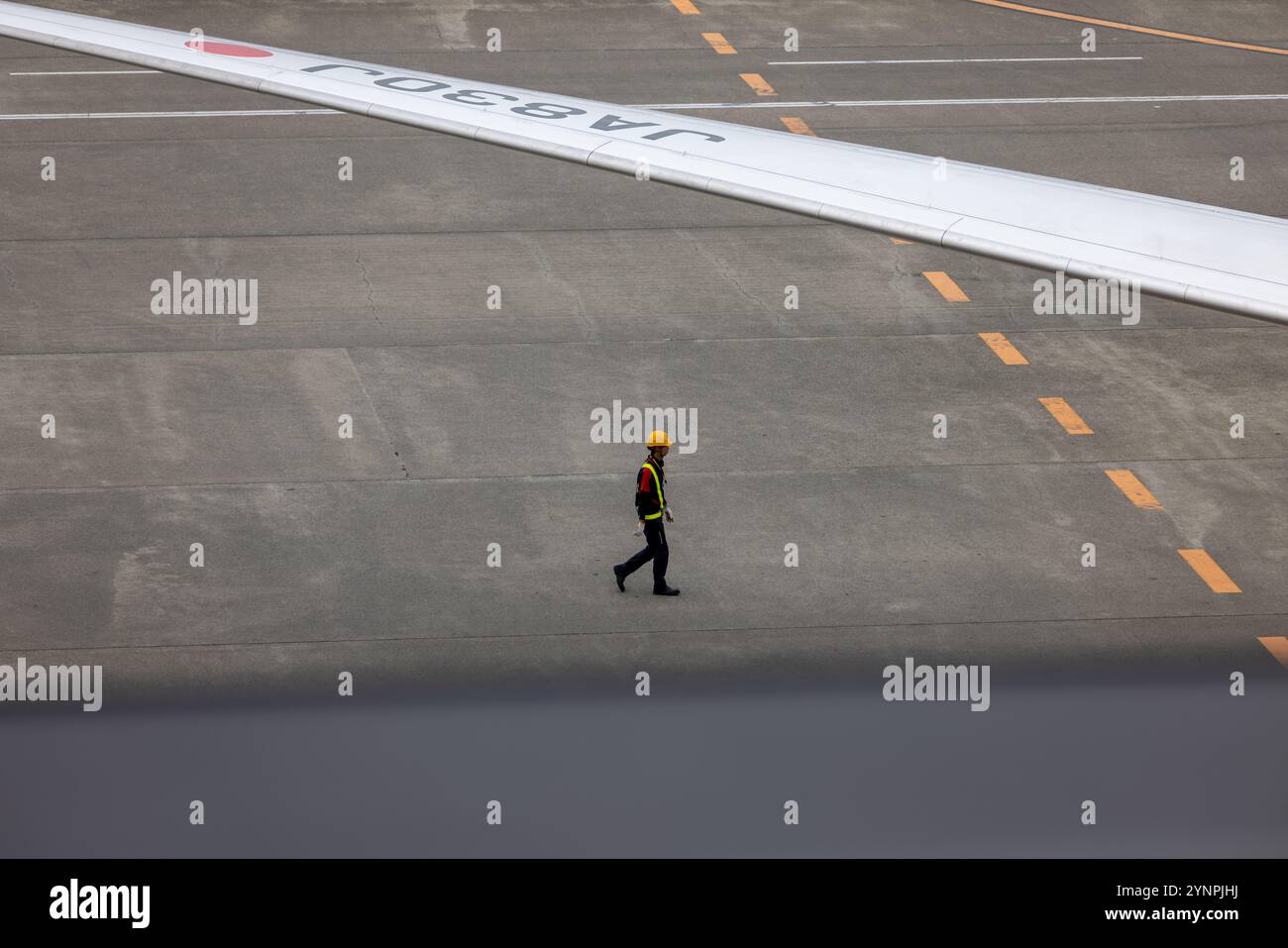 Airport ground crew member walking near an aircraft wing on the runway ...
