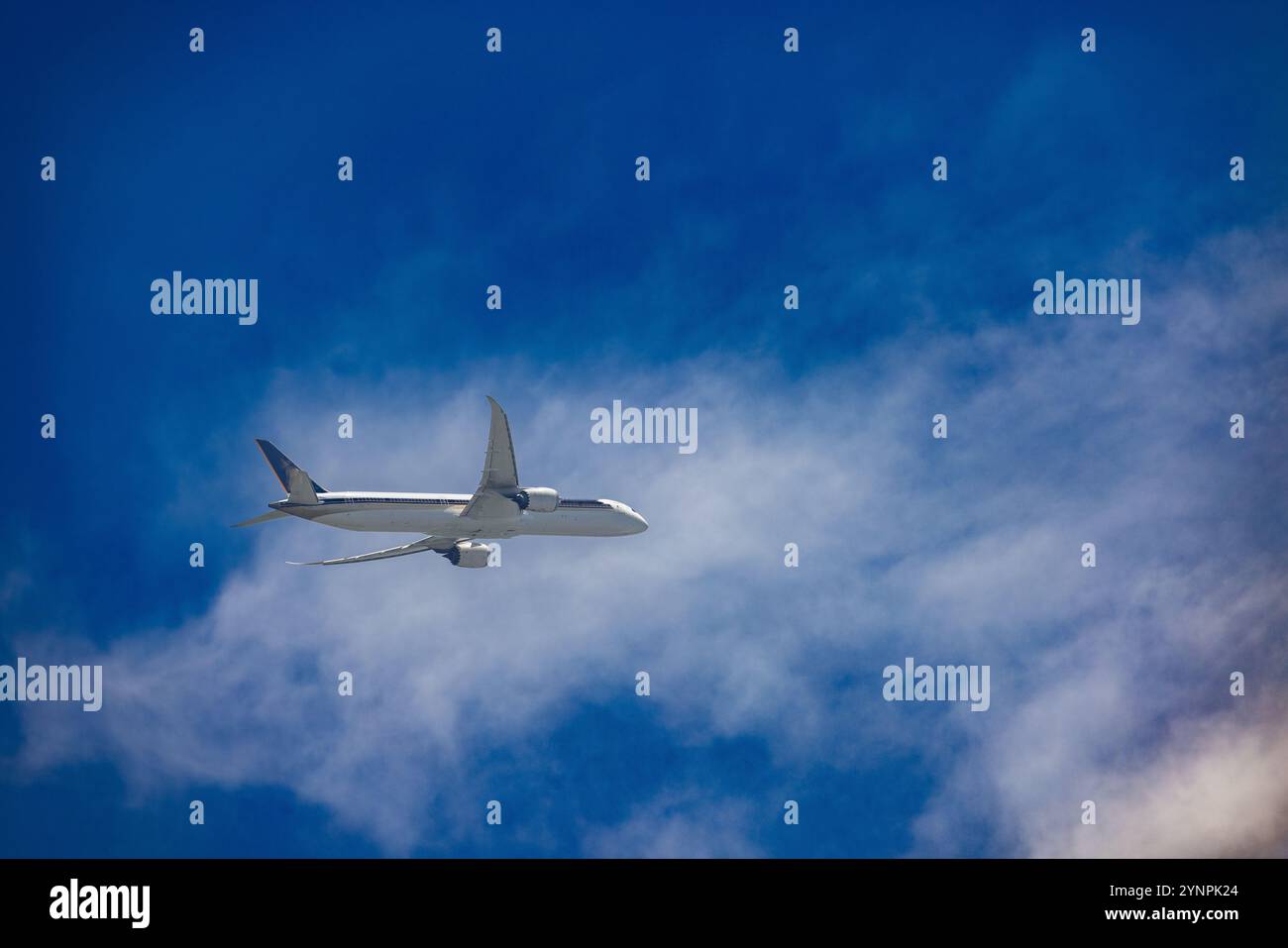 A passenger airplane cruising through a vibrant blue sky with wisps of ...