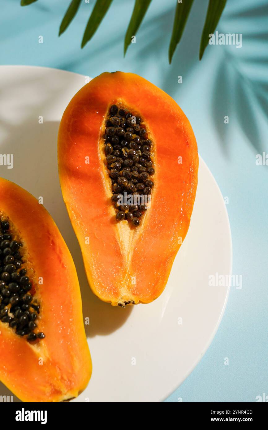 fresh, ripe papaya sliced open on light blue background, harsh sunlight ...
