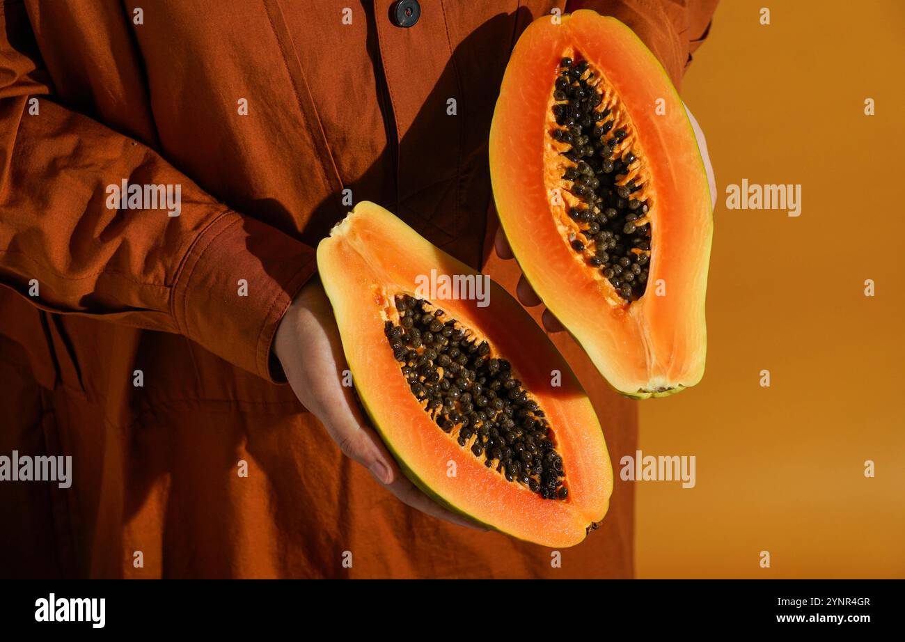 fresh, ripe papaya sliced open in woman's hands, on orange background ...