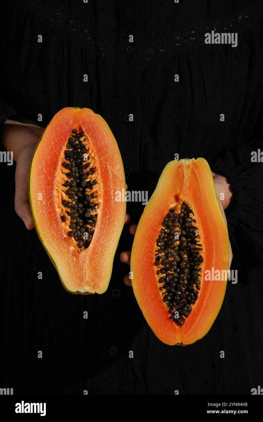 fresh, ripe papaya sliced open in woman's hands, on black background ...