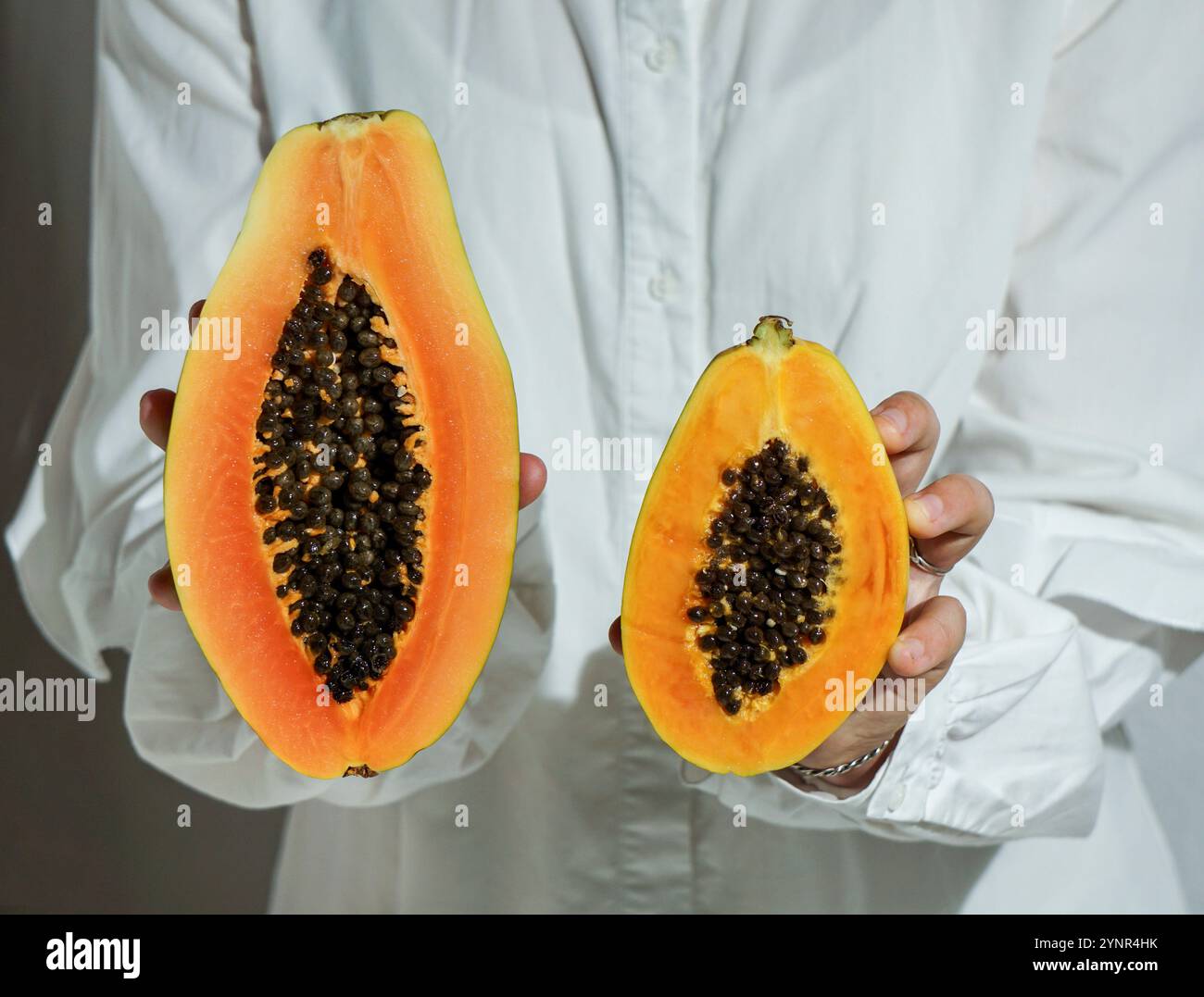 fresh, ripe papaya sliced open in woman's hands, on orange background, harsh sunlight Stock ...