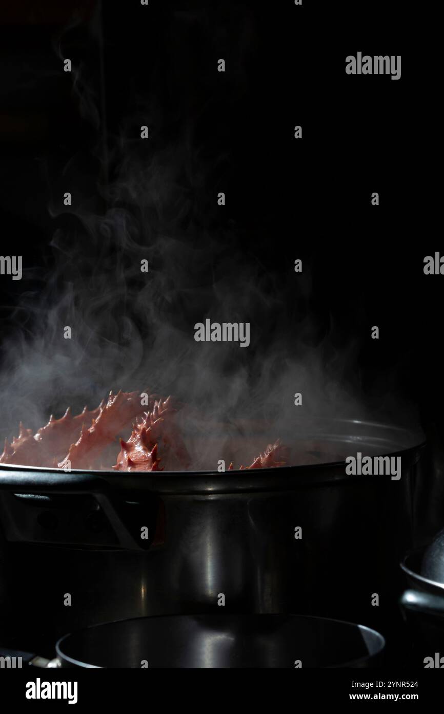 Whole king crab boiling in a metal pan, hot steam on a black background ...