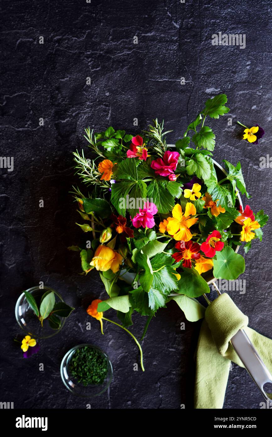 Cooking with herbs and edible flowers concept. Frypan skillet on dark ...