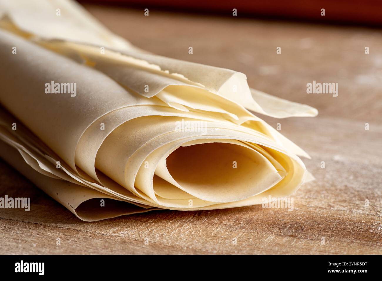On a wooden cutting board, rolled layers of phyllo dough are arranged ...