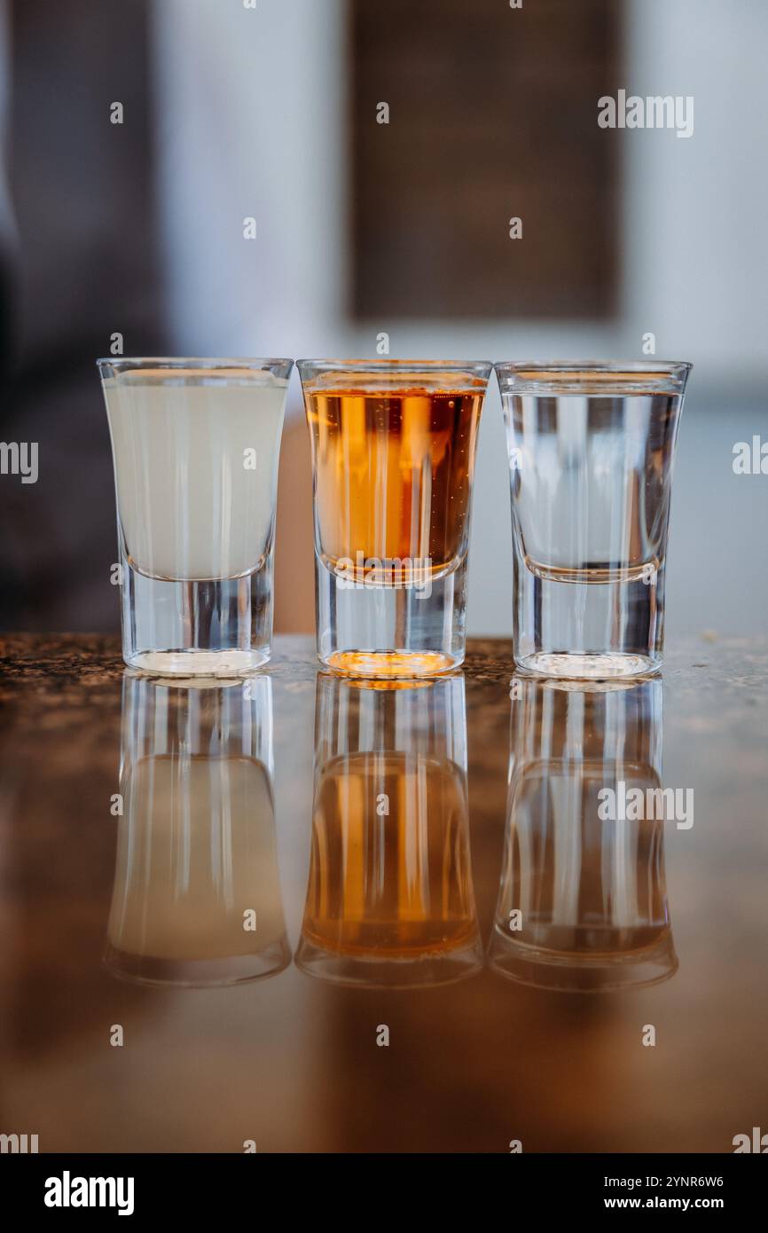Three glasses of diverse drinks reflecting on a shiny surface for a ...