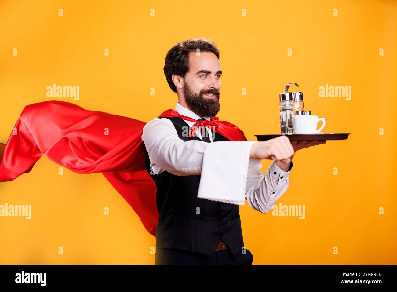 Young man server holds tray with coffee cup, wearing red cape and ...