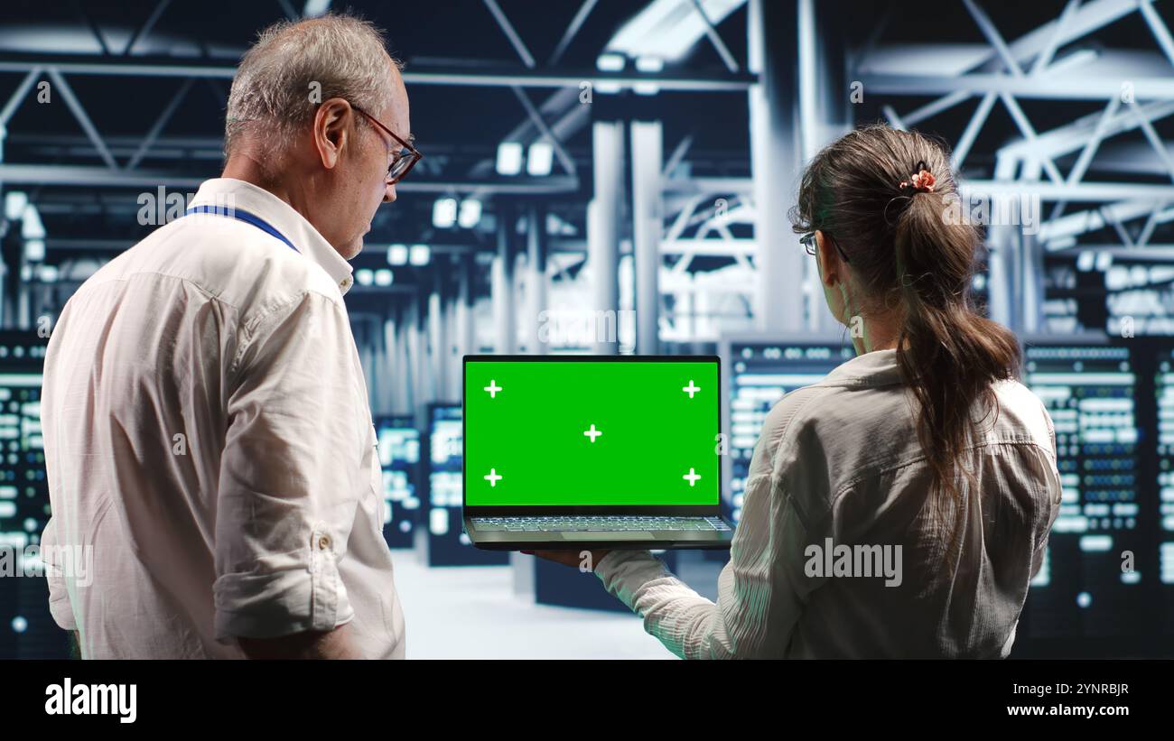 Admins using green screen laptop to monitor energy efficient data center clusters. Blade servers ...