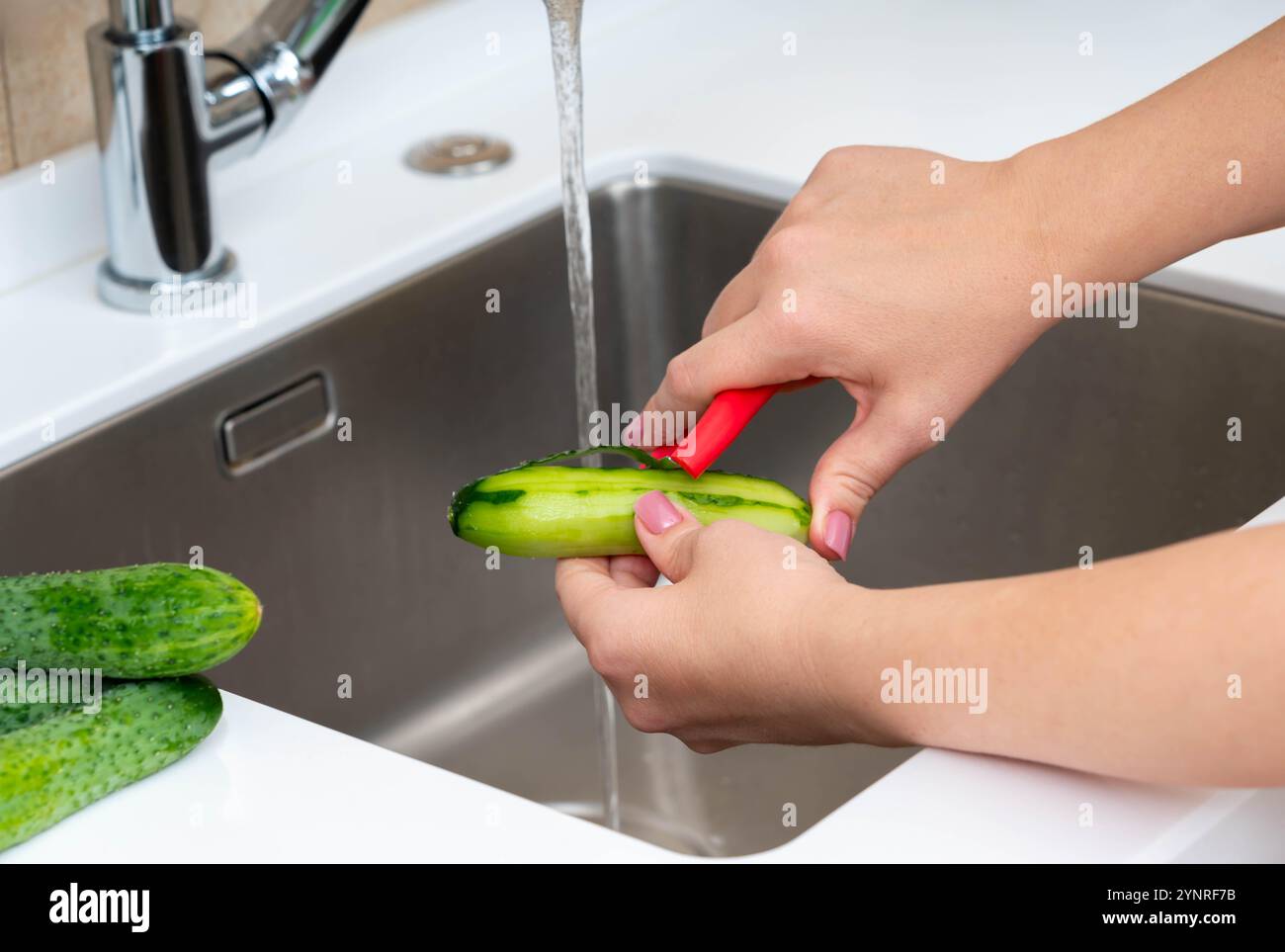 Peeling a fresh cucumber under running water in the sink, highlighting ...