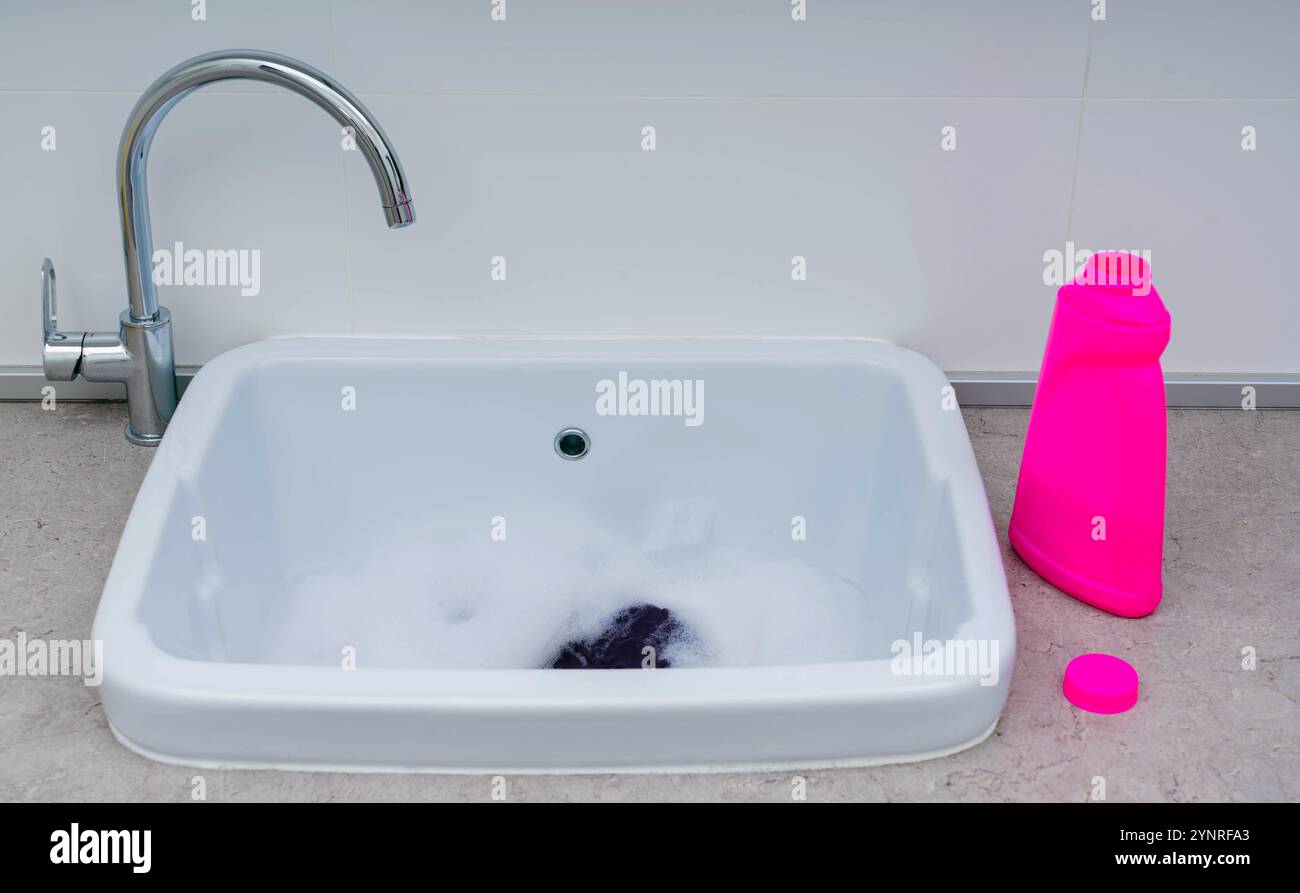 A simple handwashing setup with a pink detergent bottle and soapy water ...