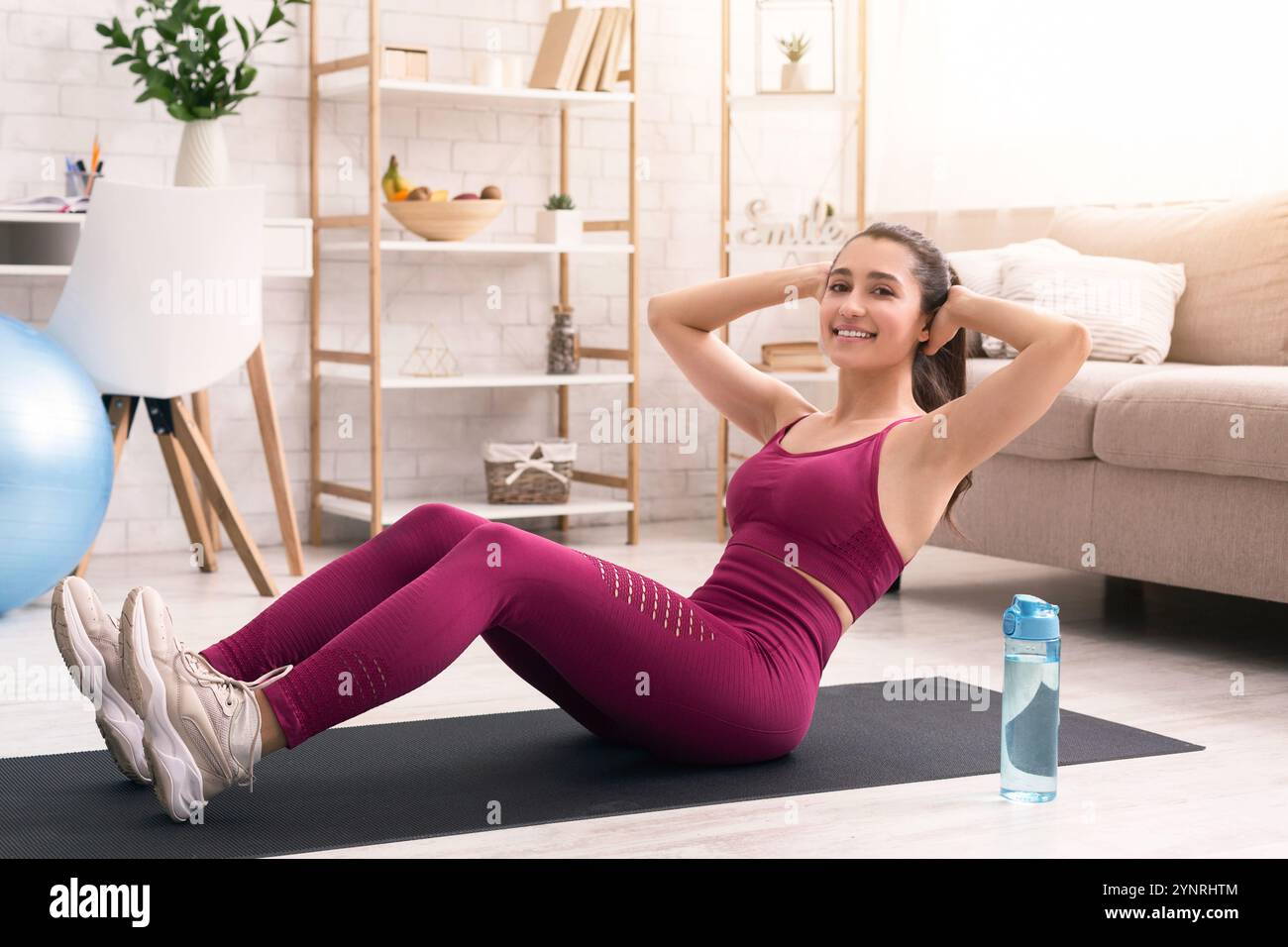 Stay at home sports. Cheerful Hispanic girl doing abs workout in light ...