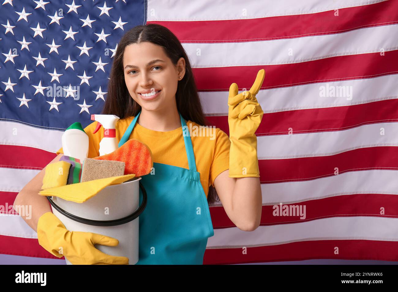 Female janitor holding bucket with cleaning supplies and pointing at ...
