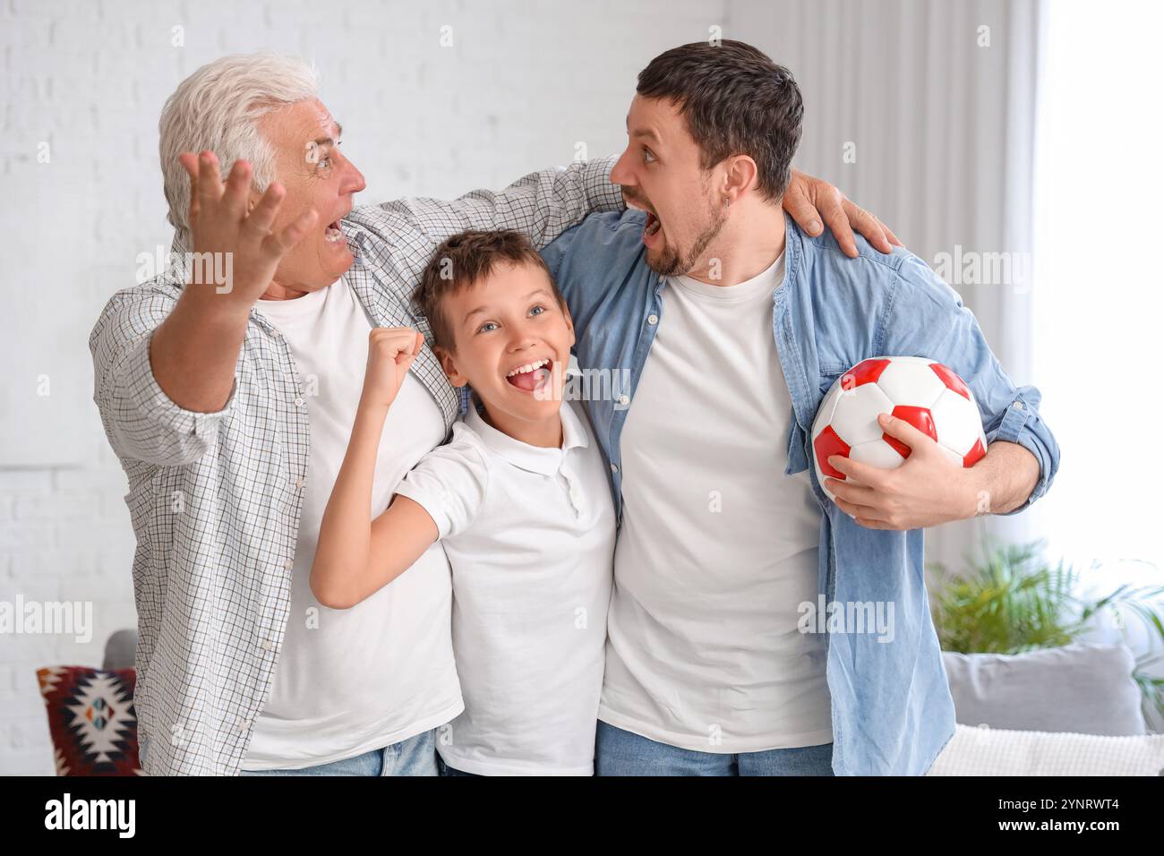 Boy with his dad and grandfather cheering for football team with soccer ...
