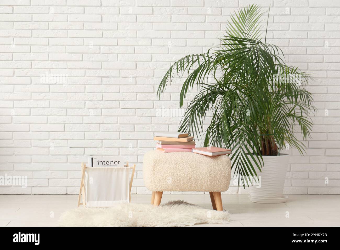 Ottoman with stack of books and houseplant near white brick wall Stock ...