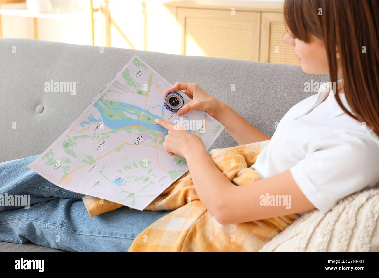 Female tourist with compass and city map lying on sofa at home, closeup ...