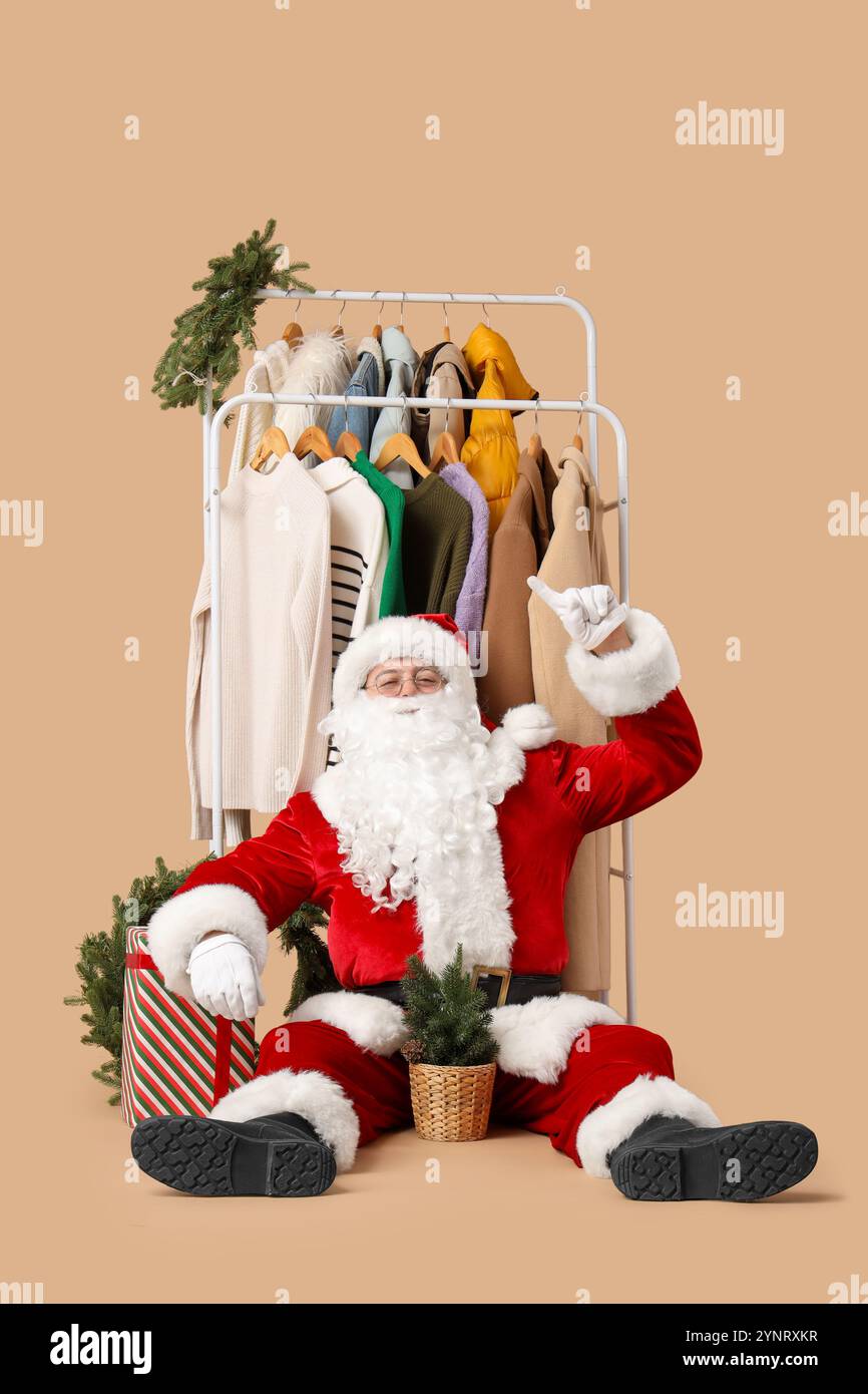 Santa Claus pointing at rack with different clothes and gift box near ...