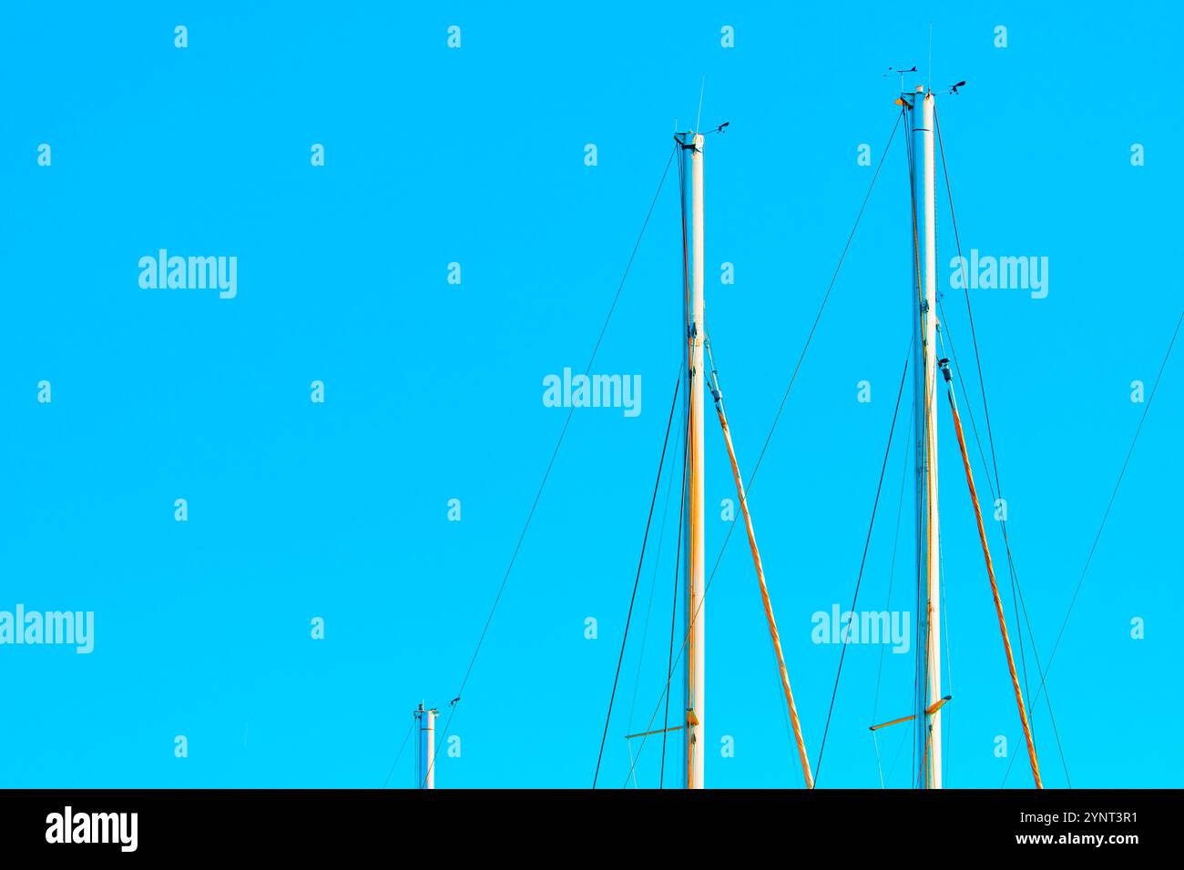 Upper parts of sailboat masts against a clear blue sky. Masts are ...