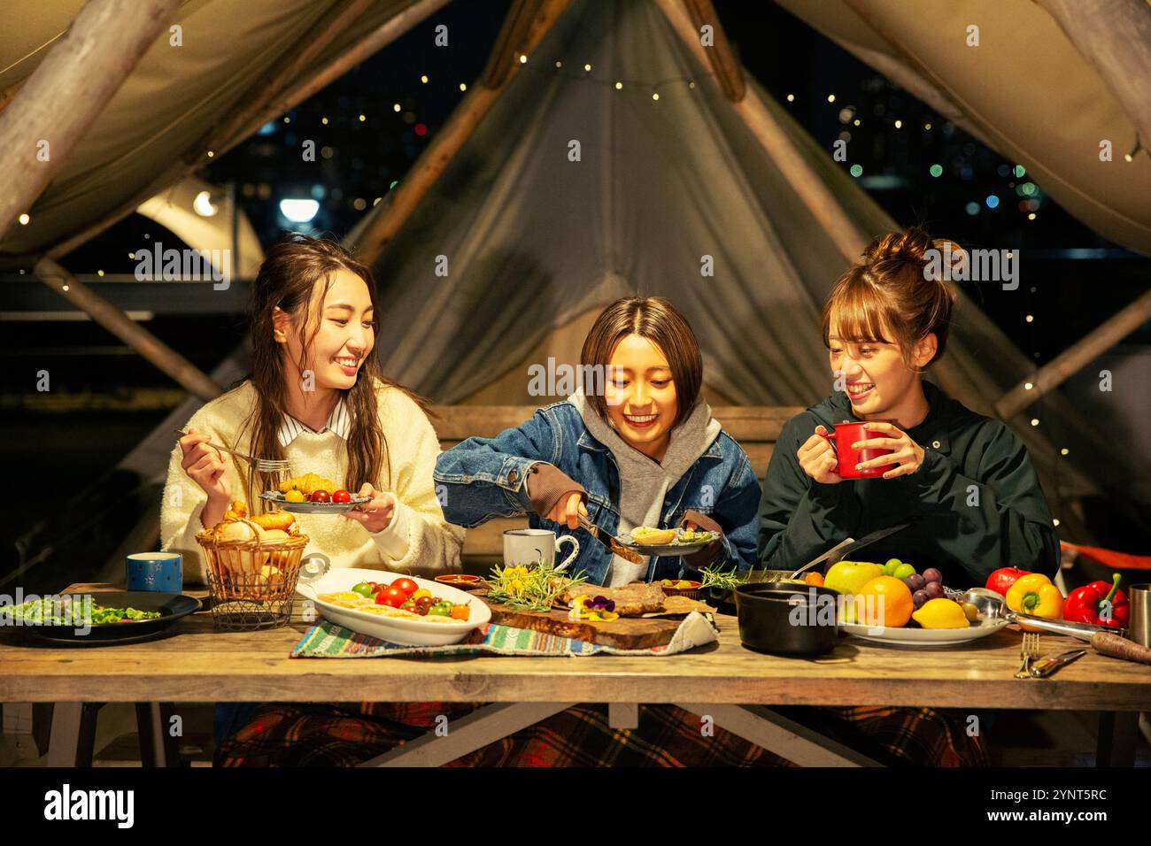 Three smiling women in their 20s having outdoor dinner Stock Photo - Alamy