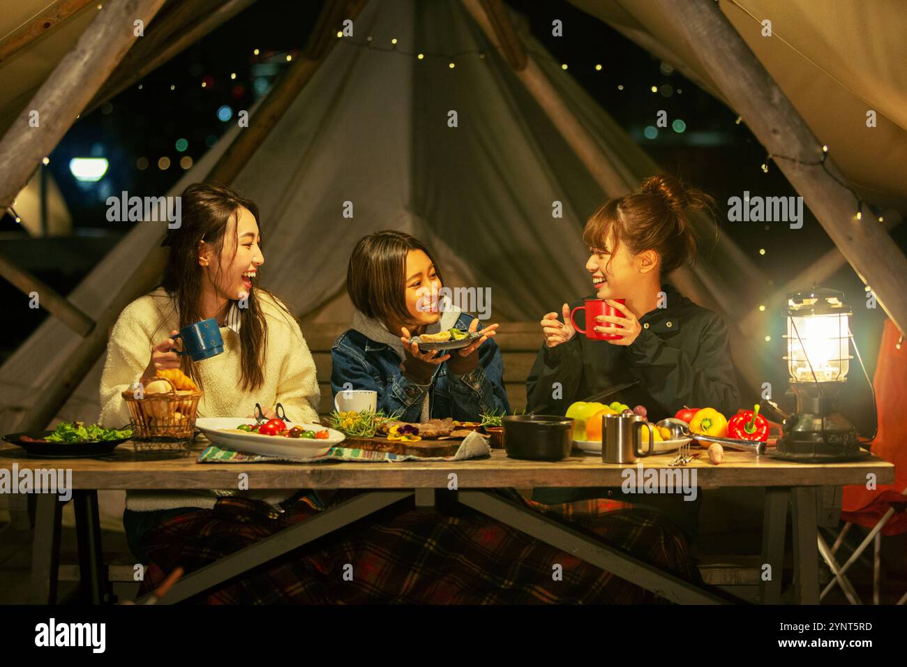Three smiling women in their 20s having outdoor dinner Stock Photo - Alamy