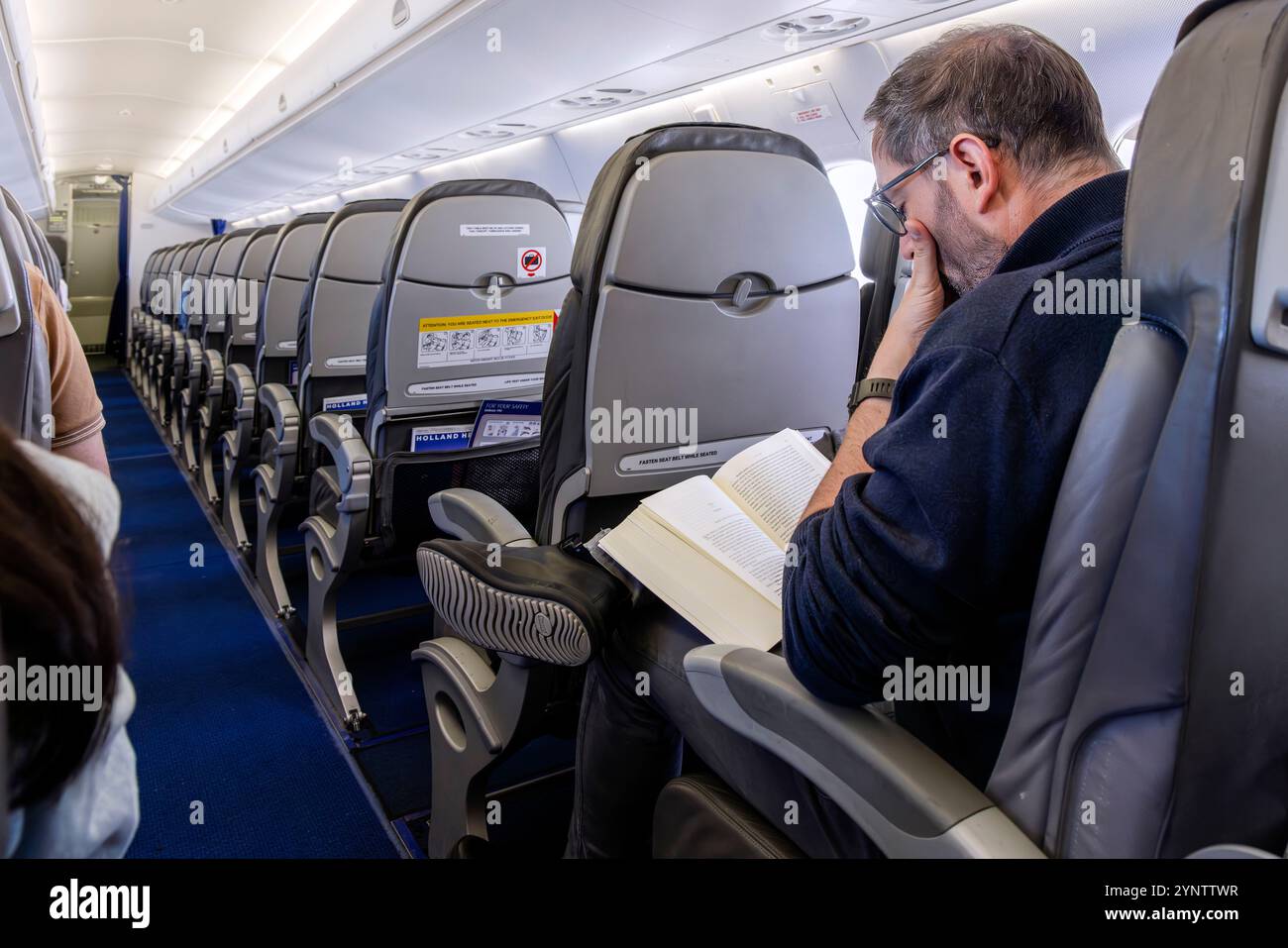 Cabin interior, passenger reading book, onboard flight from UK to ...