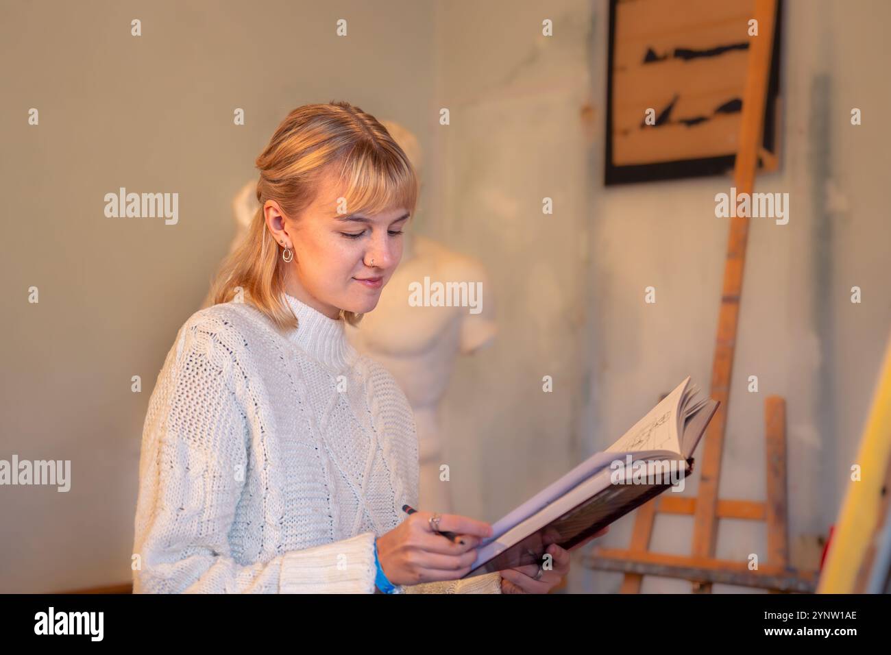Young attractive female artist reading an anatomy book. Learning ...