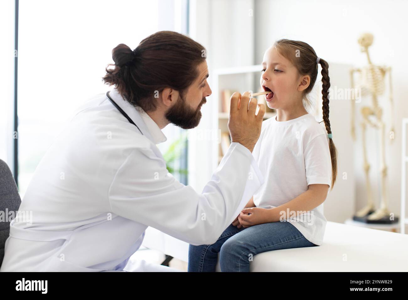 Caucasian male doctor examines throat of girl with tongue depressor in ...