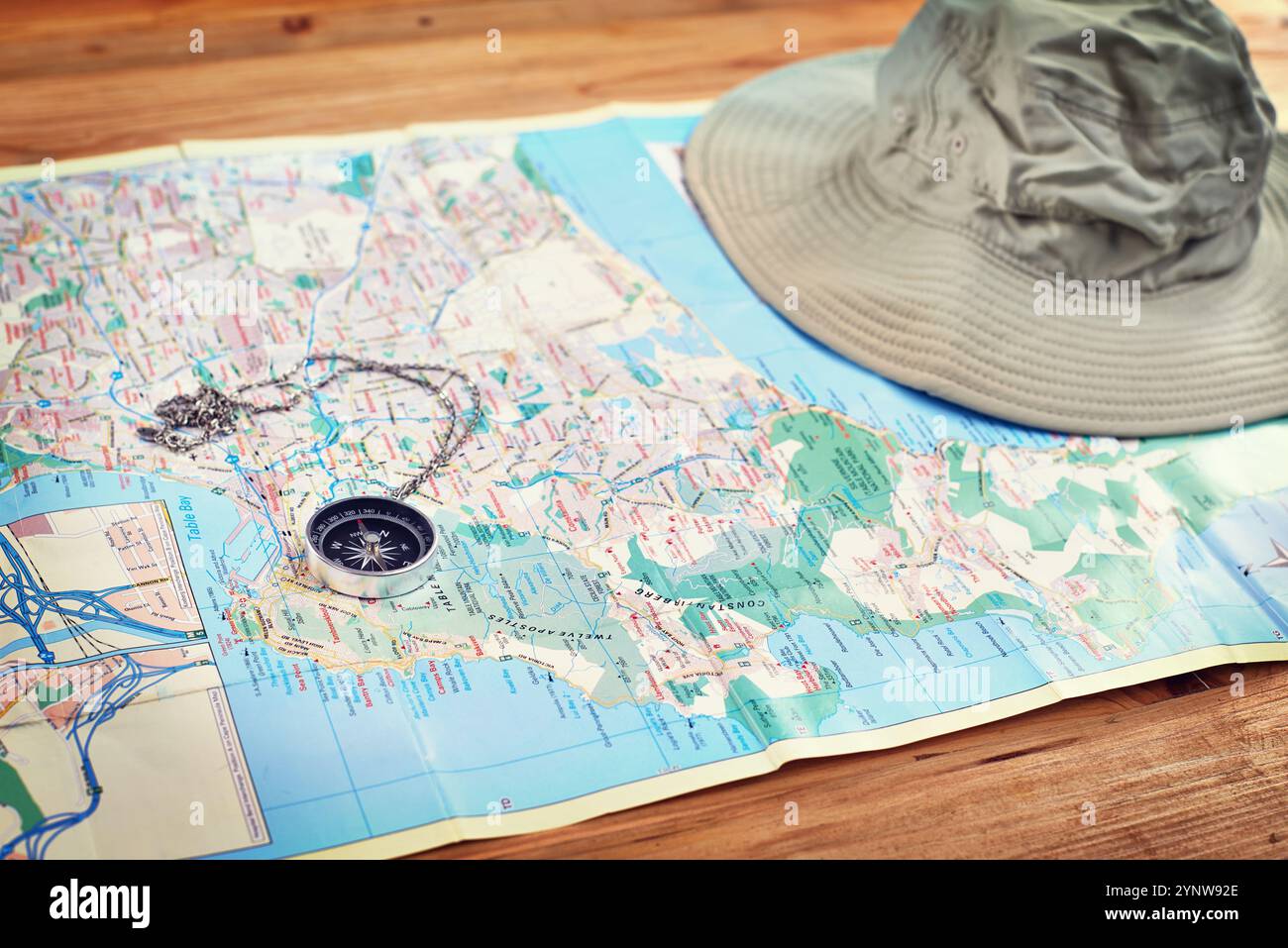 Hat, map and travel guide with compass on table for itinerary schedule ...