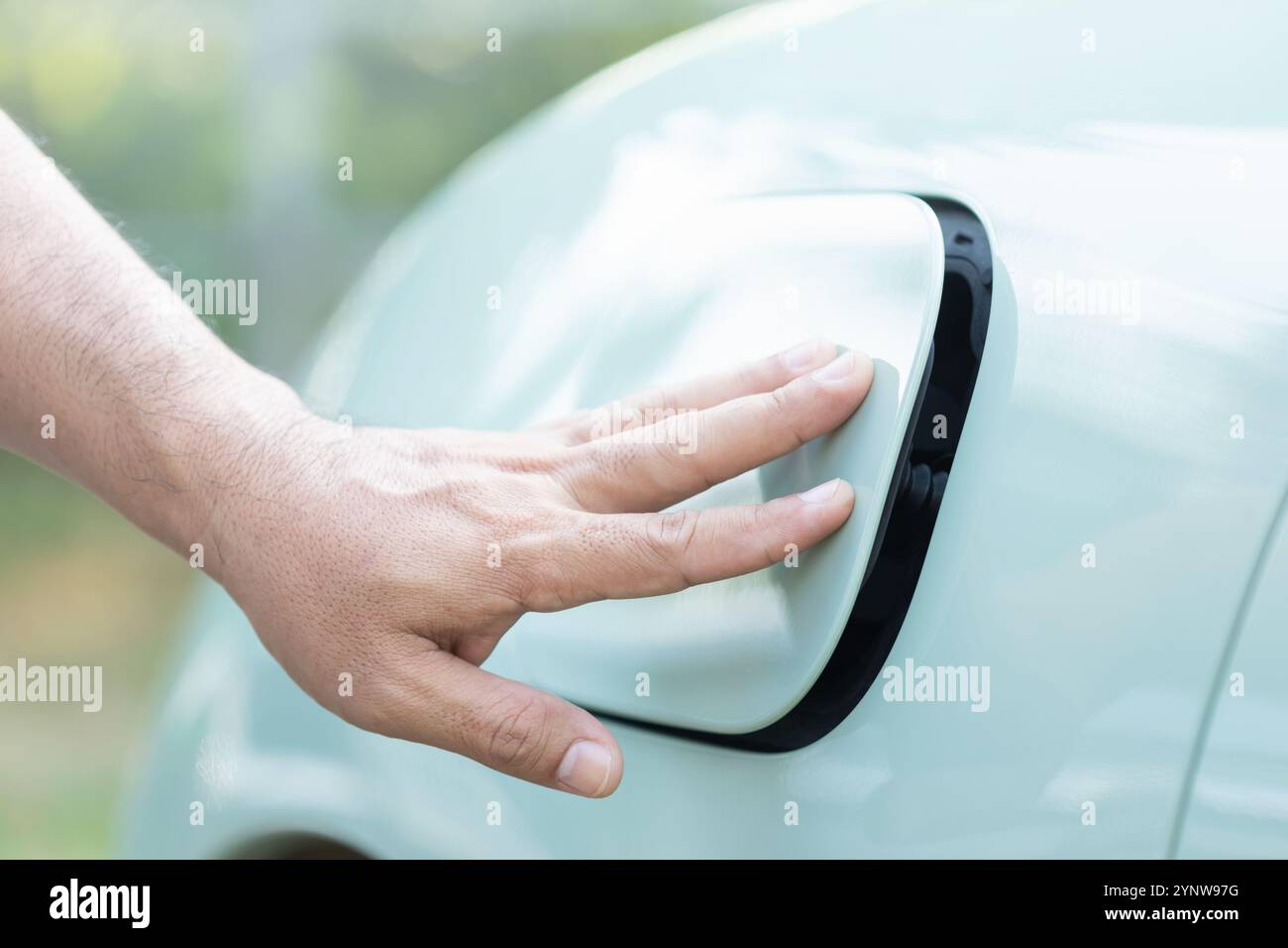 Car owner's hand gently touches the charging port cover of an electric ...