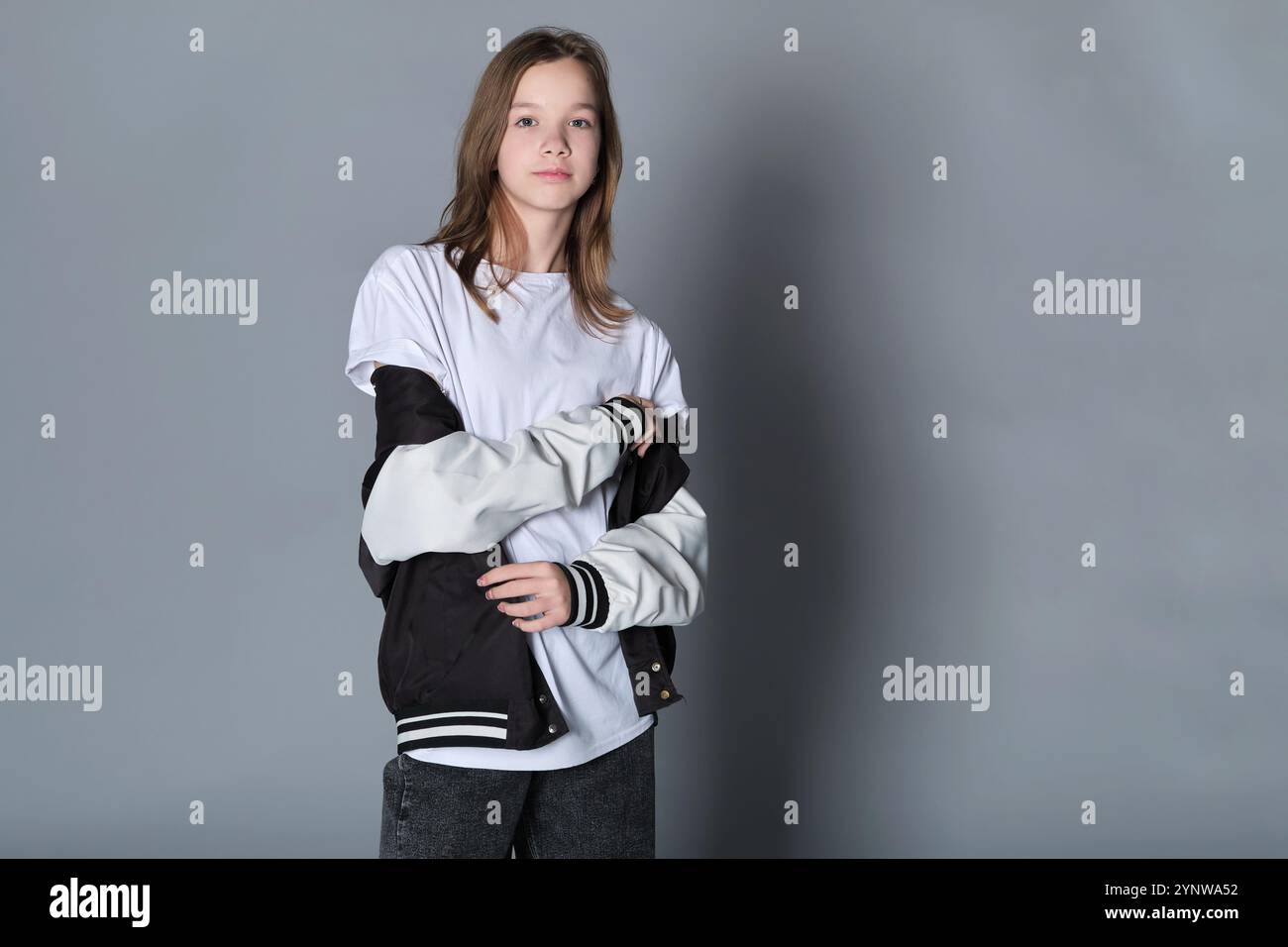 A girl stands in a relaxed pose with her jacket over her shoulders ...