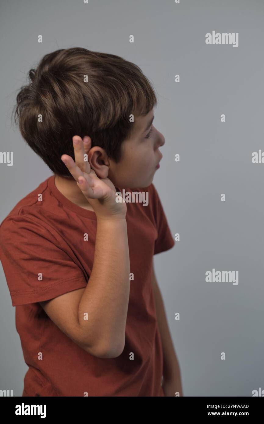 boy attentively listens, hand to ear, a gesture of focus. This image ...