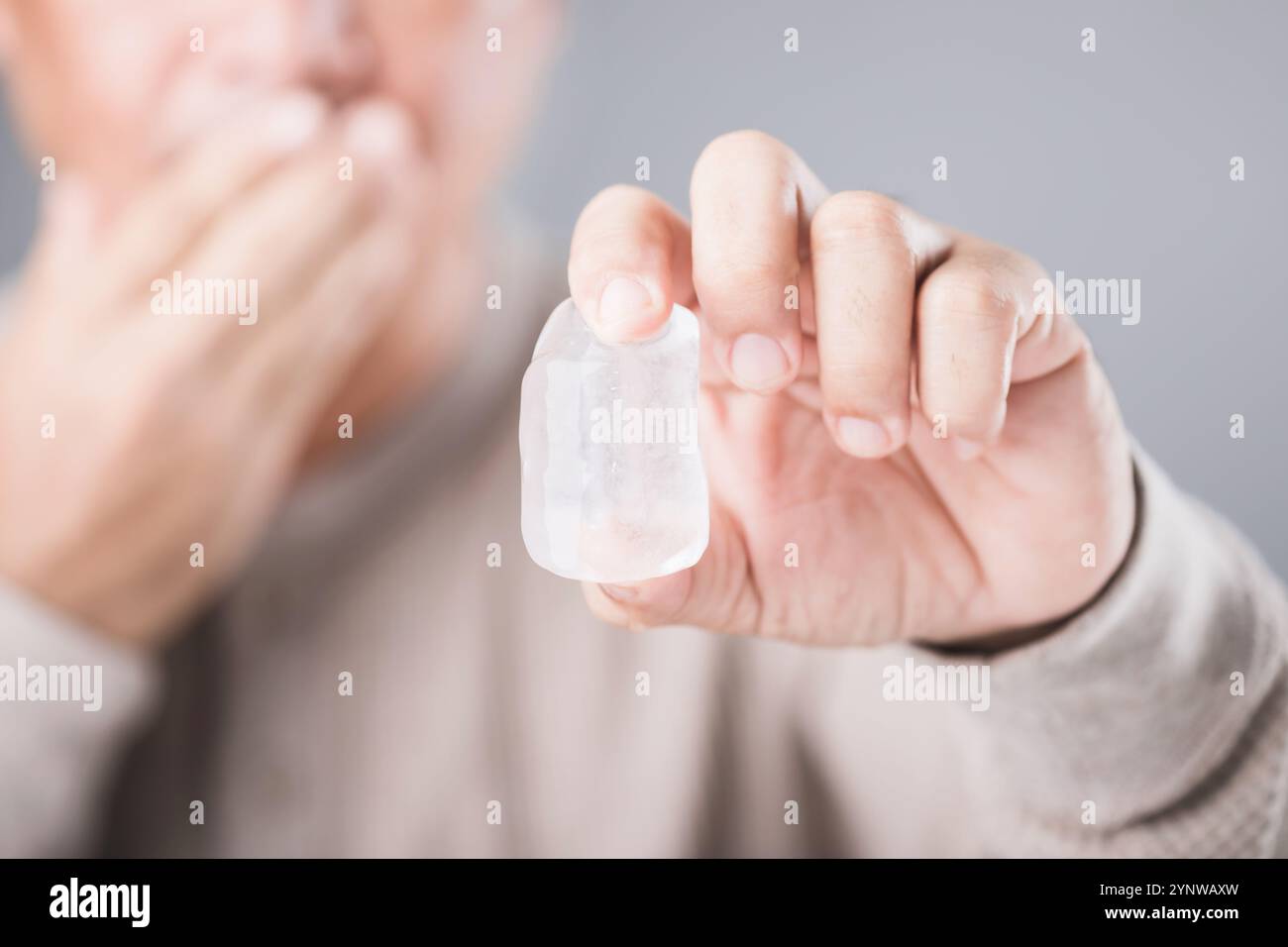 A man holding an ice cube, with a look of discomfort due to the cold ...