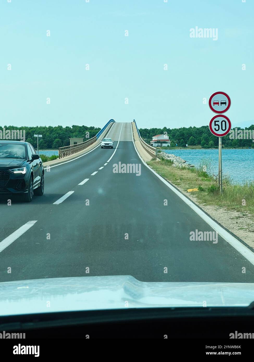 A stretch of asphalt road with cars traveling under a clear blue sky. A ...