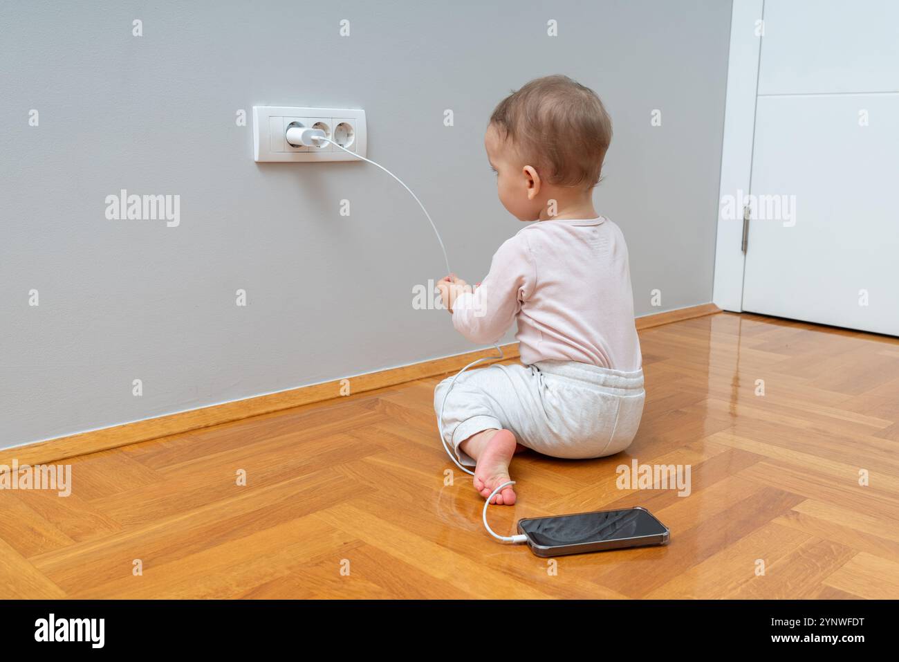 A curious toddler interacting with an electric socket and phone charger ...