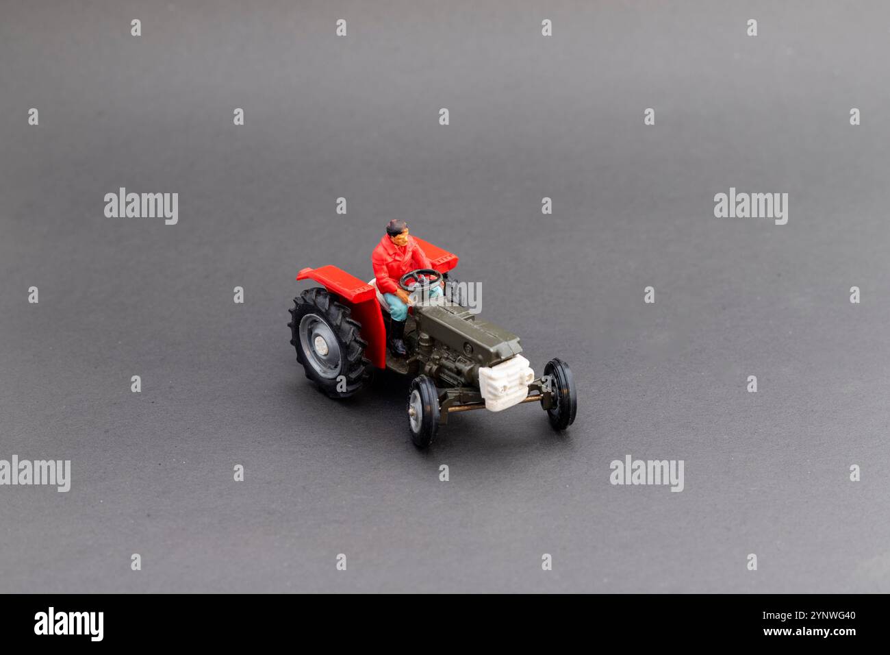 Red toy tractor with a driver on a grey background with copy space ...
